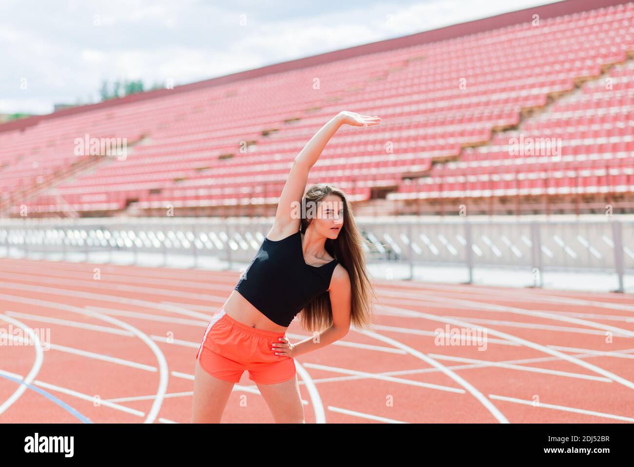 A female coach with dark hair stands on the red running track of the ...