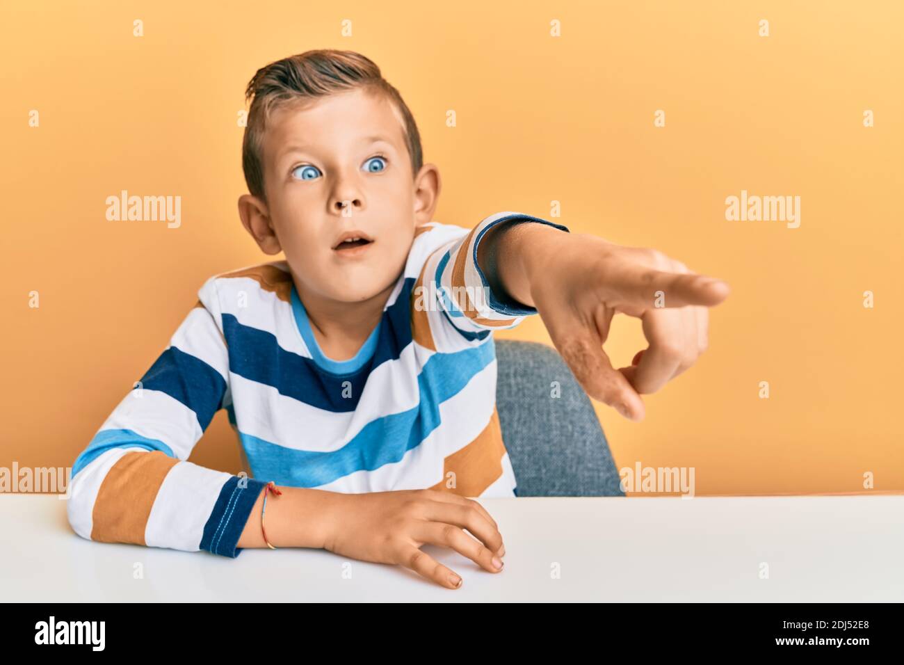 Adorable caucasian kid wearing casual clothes sitting on the table ...