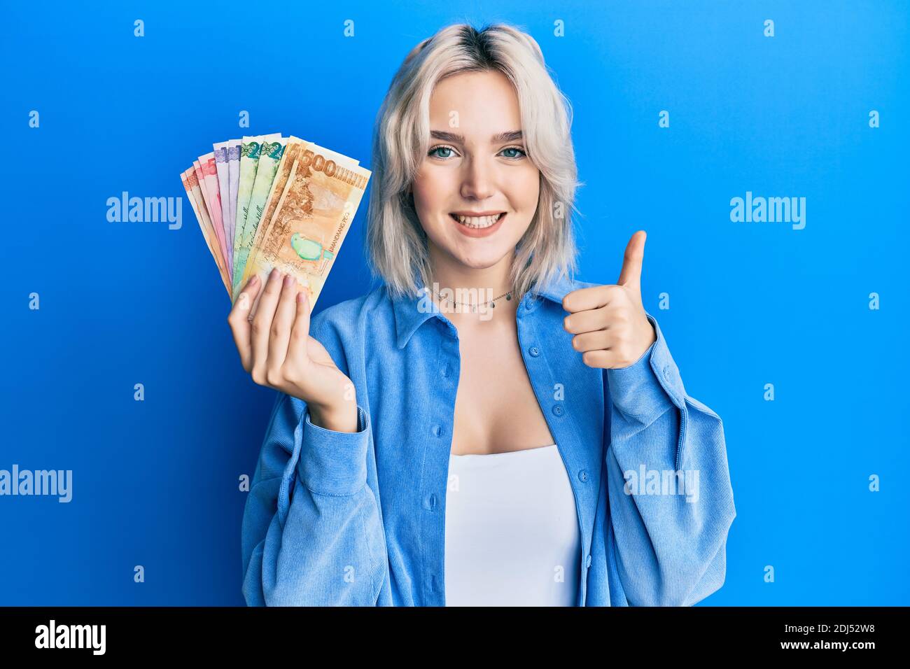 Young blonde girl holding philippine peso banknotes smiling happy and ...
