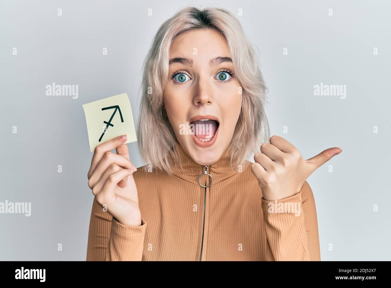 Young blonde girl holding paper with sagittarius zodiac sign pointing ...