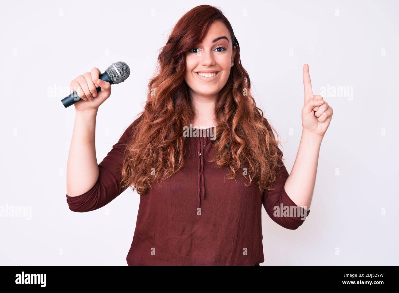 Young beautiful woman singing song using microphone smiling with an ...