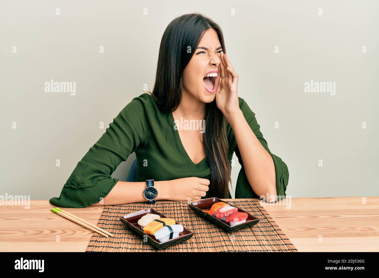 Young brunette woman eating sushi sitting on the table shouting and ...