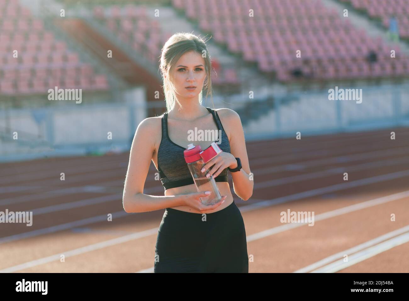A female coach with dark hair stands on the red running track of the ...