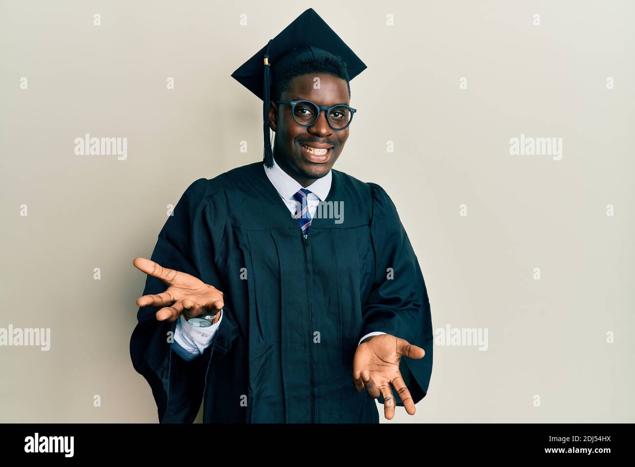 Handsome black man wearing graduation cap and ceremony robe smiling ...
