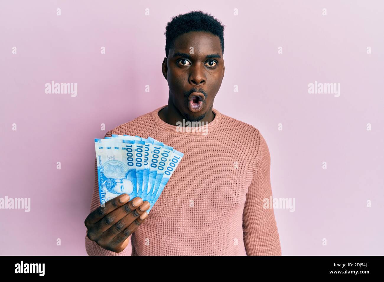 Handsome black man holding 10000 chilean pesos scared and amazed with ...