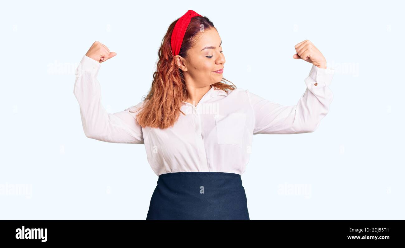 Young latin woman wearing waitress apron showing arms muscles smiling ...