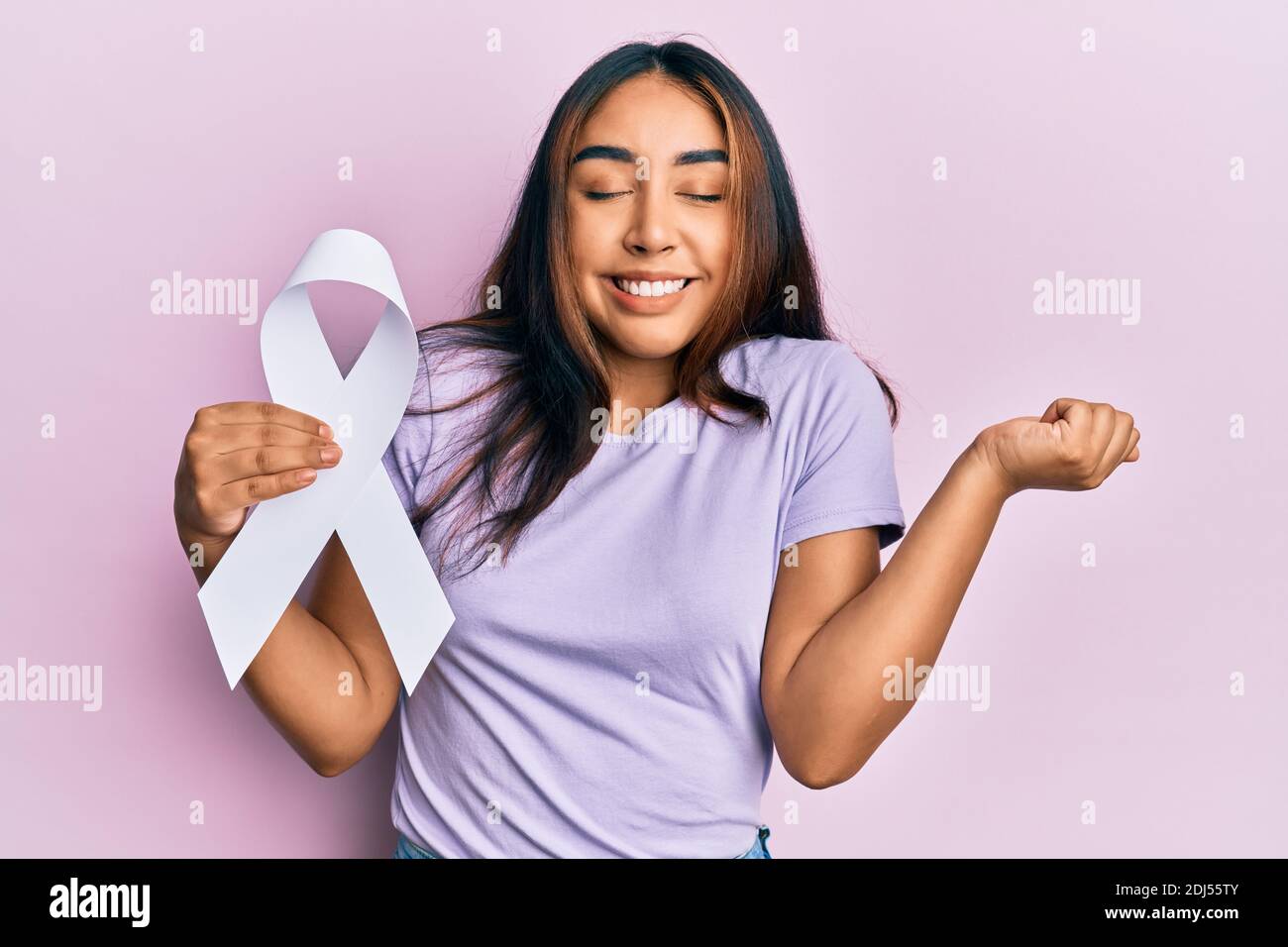 Young latin woman holding cancer awareness white ribbon screaming proud ...