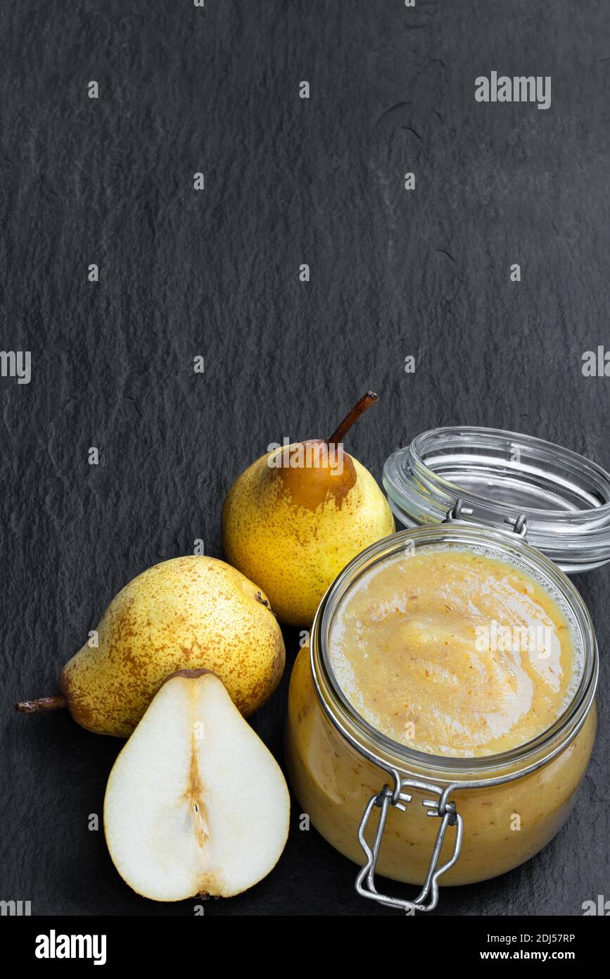 Homemade pear puree in glass jar with fresh ripe pears on black stone ...