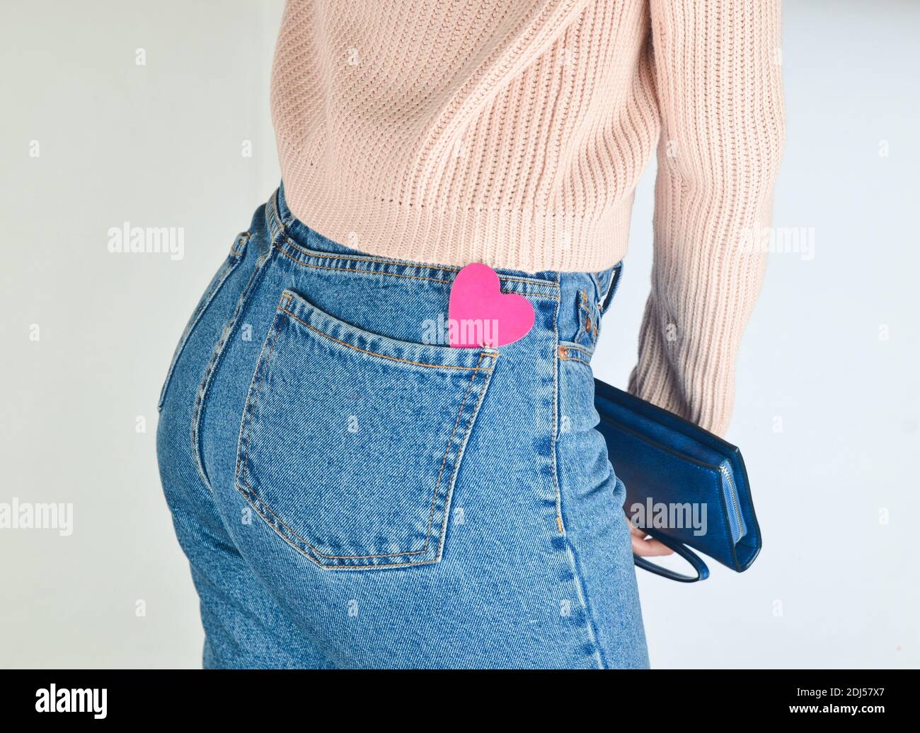 Decorative heart in the back pockets of jeans of a slim girl who holds ...