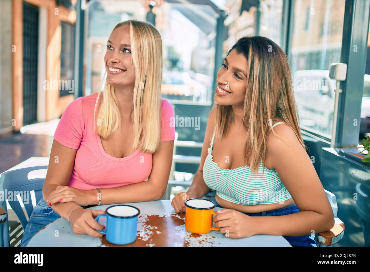 Two beautiful and young girl friends together having fun at cafeteria ...