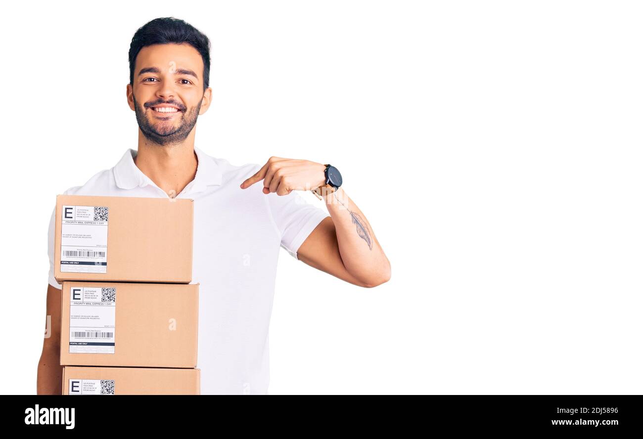 Young handsome hispanic man holding delivery package pointing finger to ...