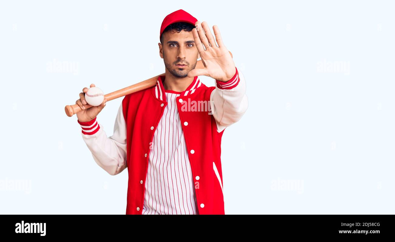 Young hispanic man playing baseball holding bat and ball with open hand ...