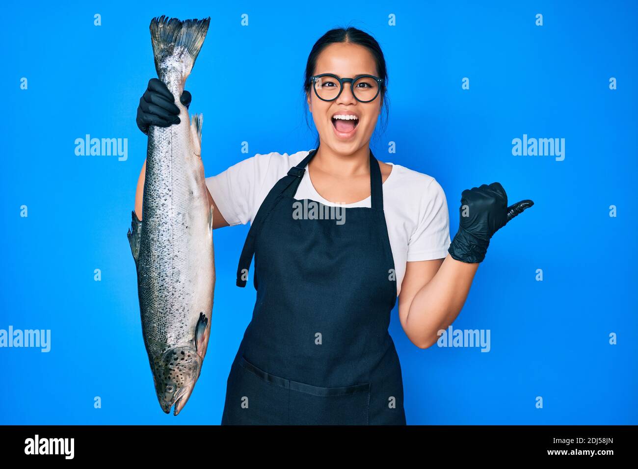 Young beautiful asian girl fishmonger selling fresh raw salmon pointing ...