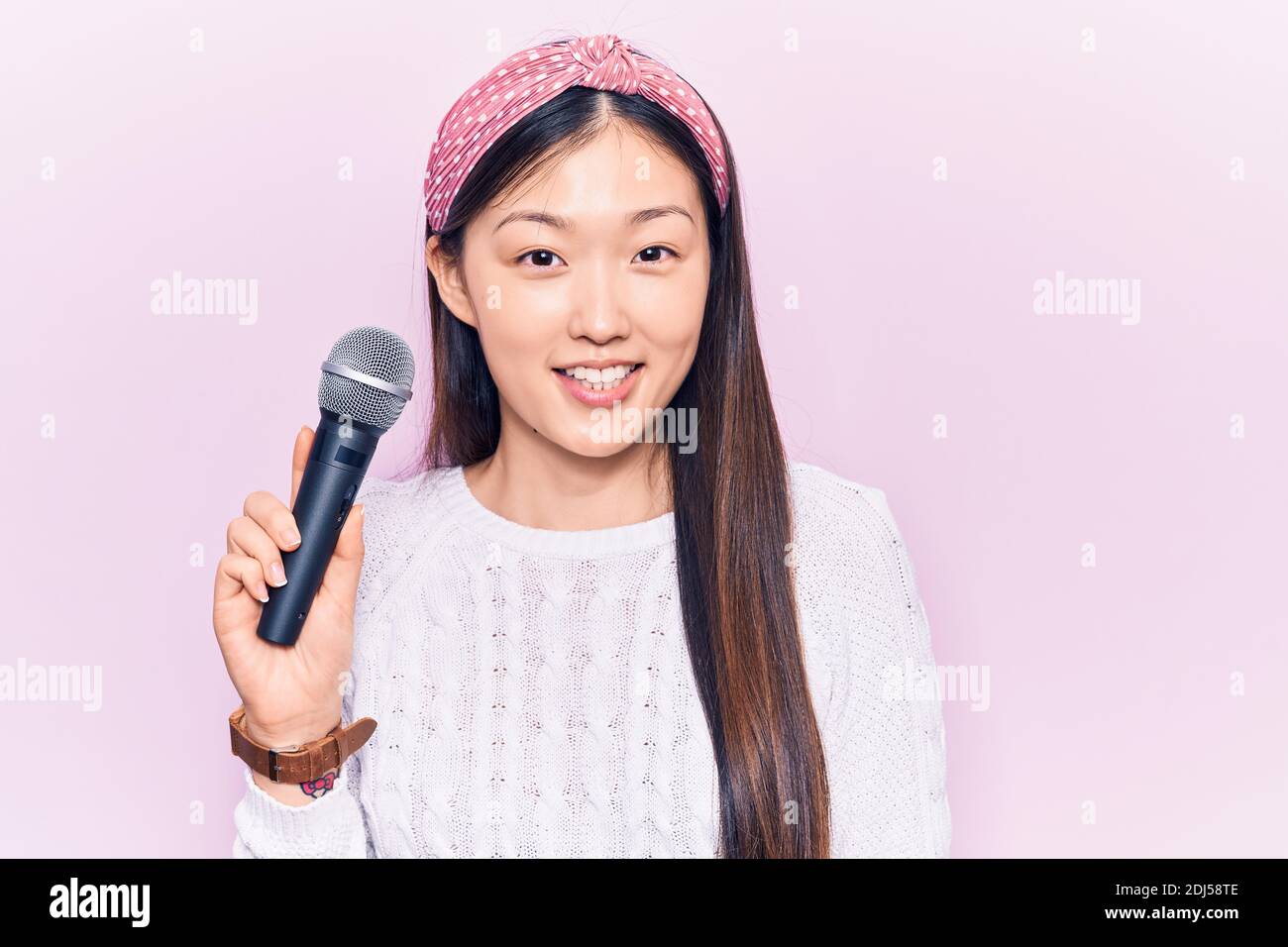 Young beautiful chinese woman singing song using microphone looking ...