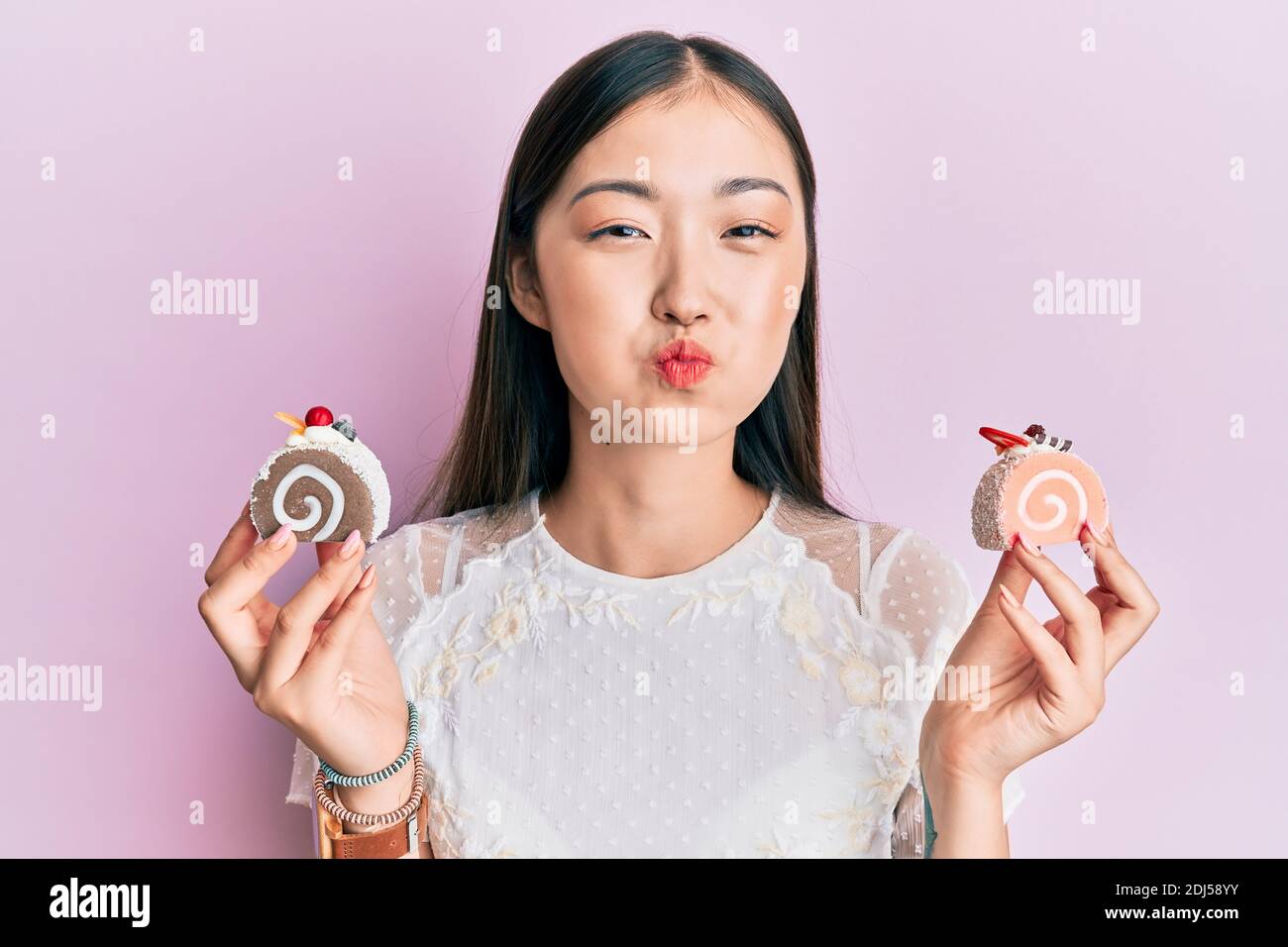 Young chinese woman holding cake sweets puffing cheeks with funny face ...