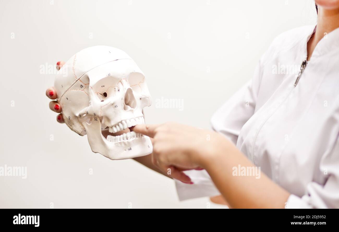 Woman in a medical uniform holding a human skull in a hands and stuck ...
