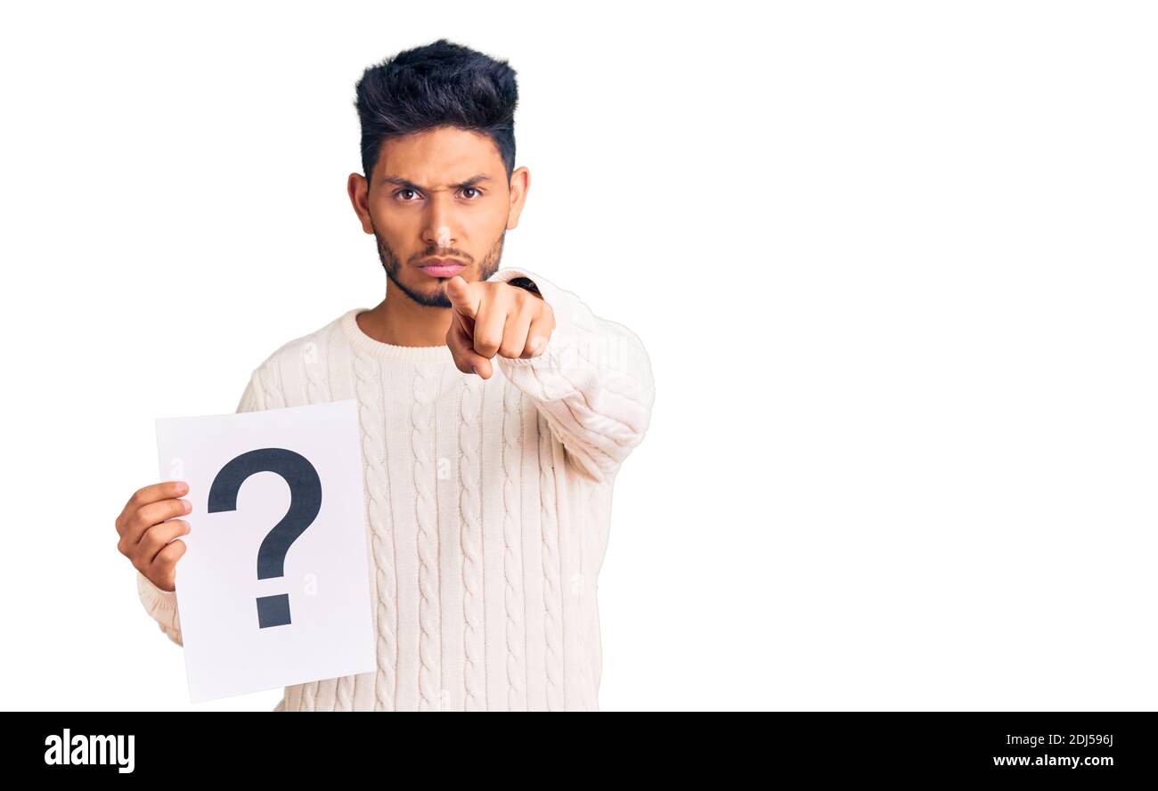 Handsome latin american young man holding question mark pointing with ...