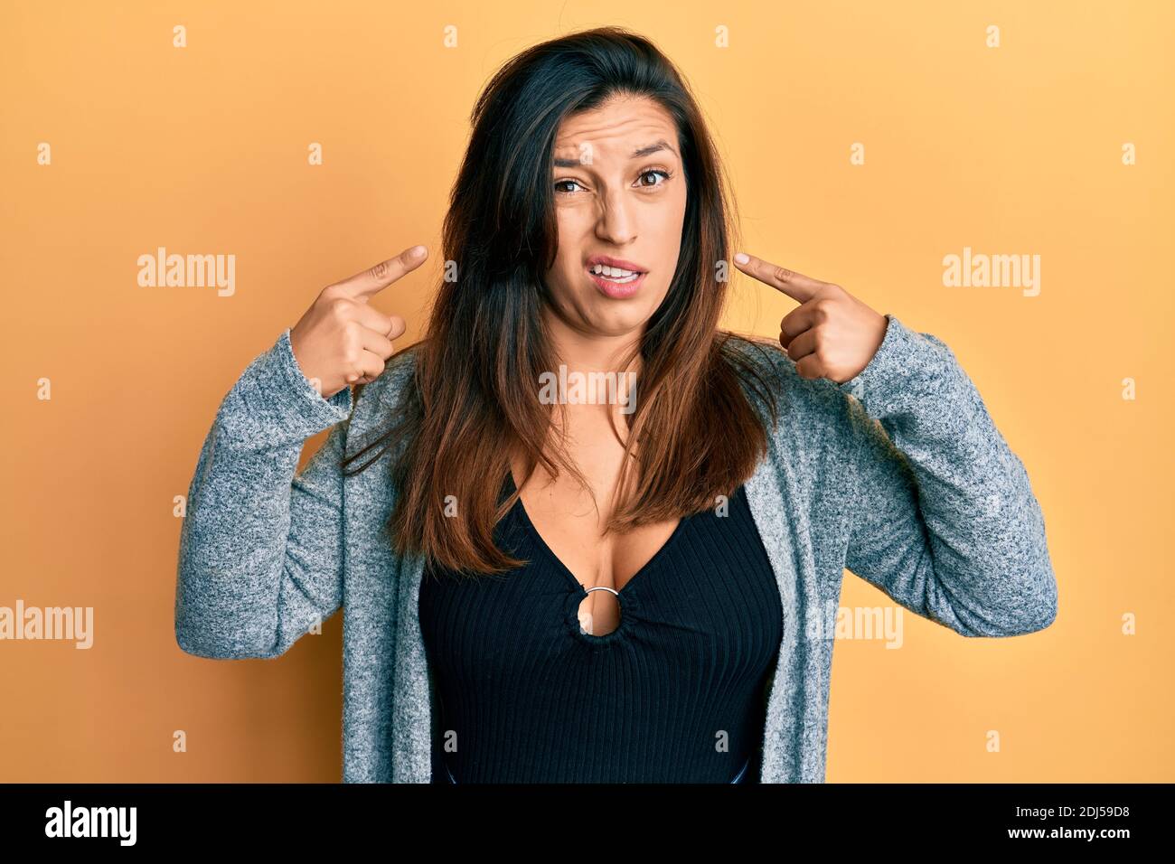 Beautiful hispanic woman pointing to mouth with fingers clueless and ...