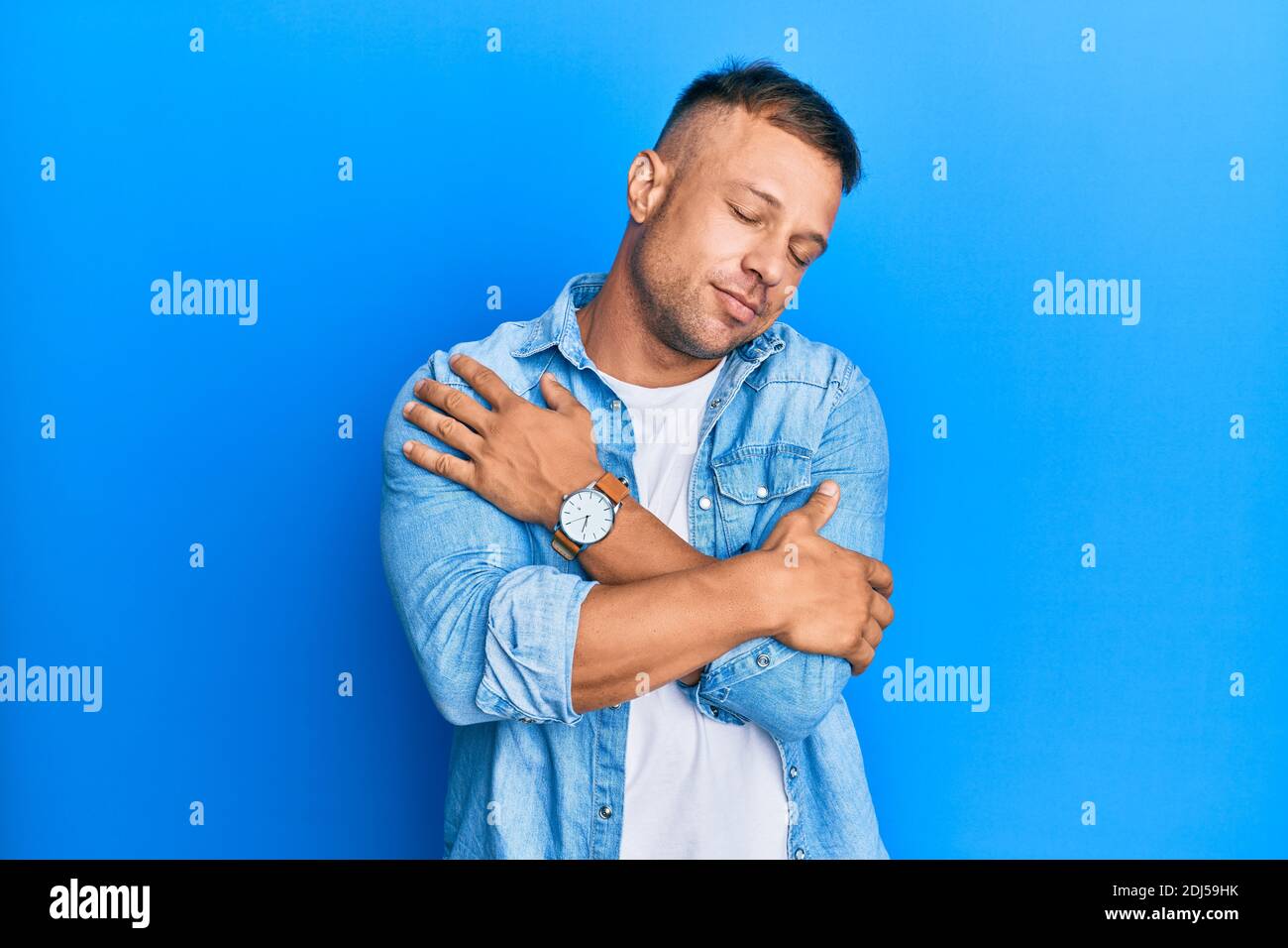 Handsome muscle man wearing casual denim jacket hugging oneself happy ...