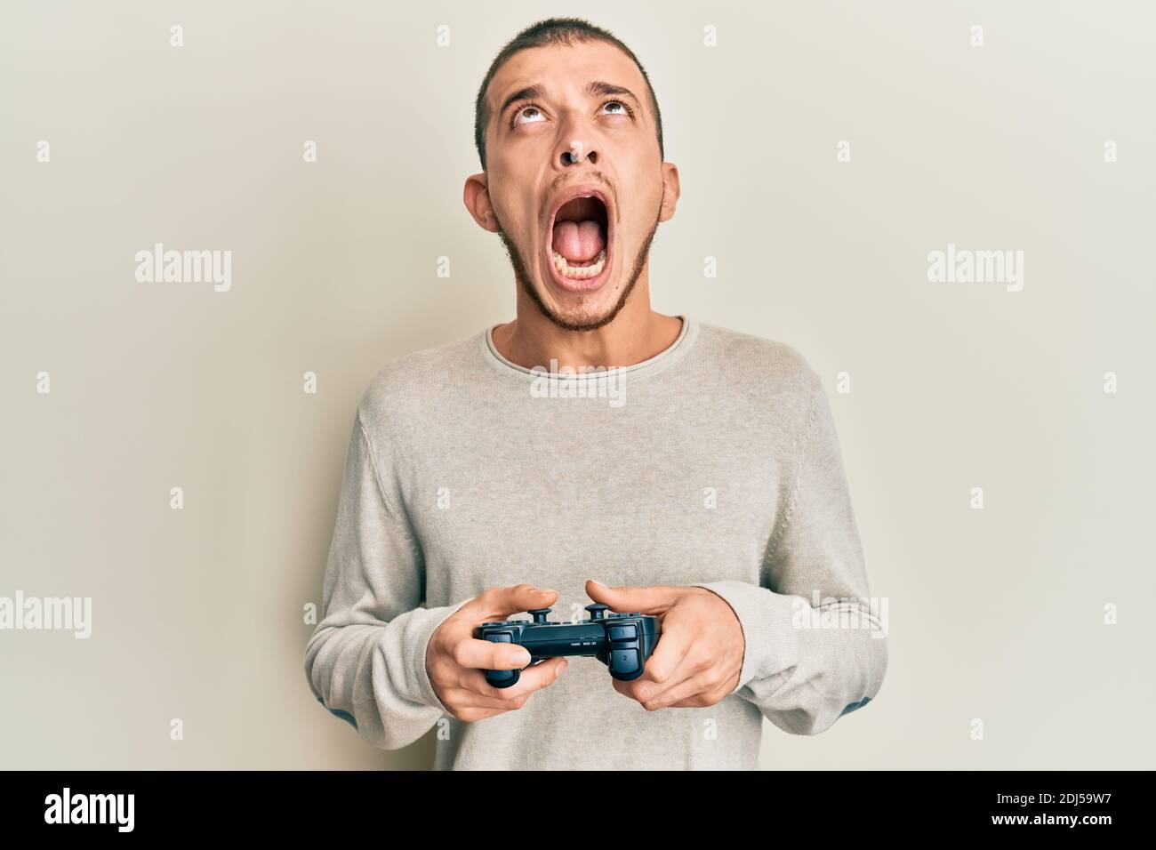 Hispanic young man playing video game holding controller angry and mad ...