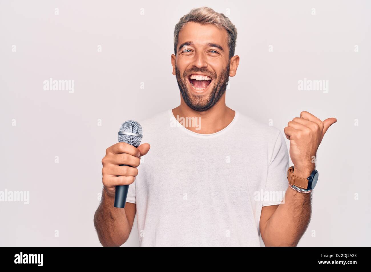 Handsome blond singer man with beard singing song using microphone over white background ...