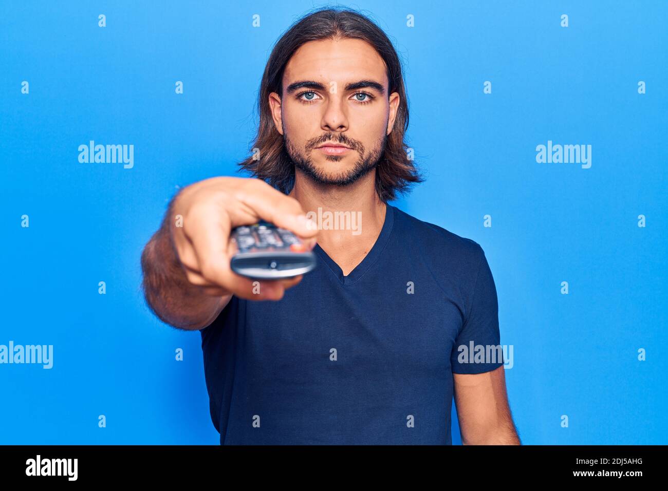 Young handsome man holding television remote control thinking attitude ...