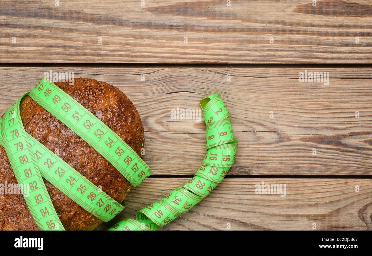 A loaf of bran bread wrapped with a ruler on a wooden background. The ...