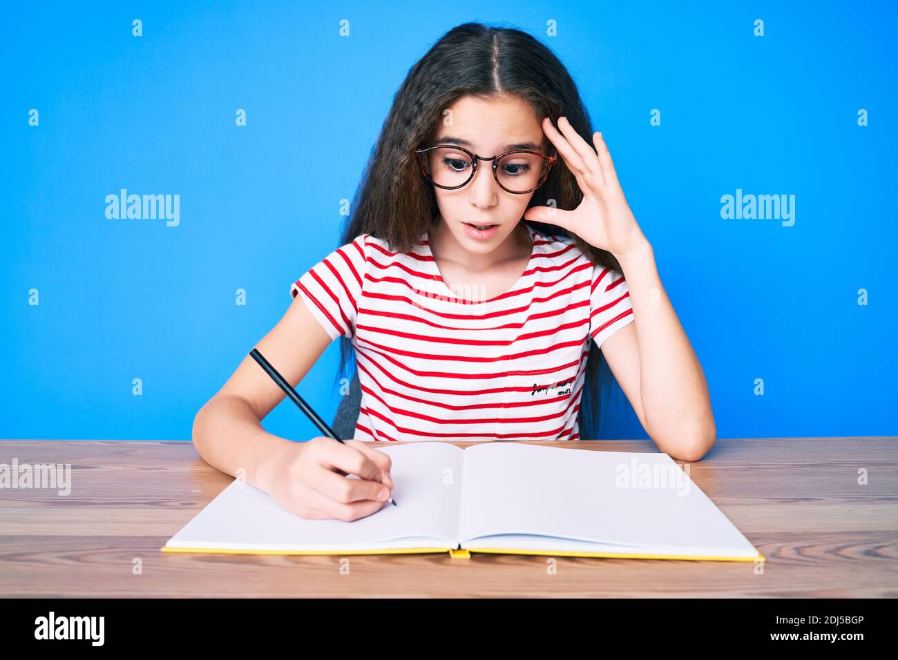 Cute hispanic child girl sitting on the table writing book stressed and frustrated with hand on ...