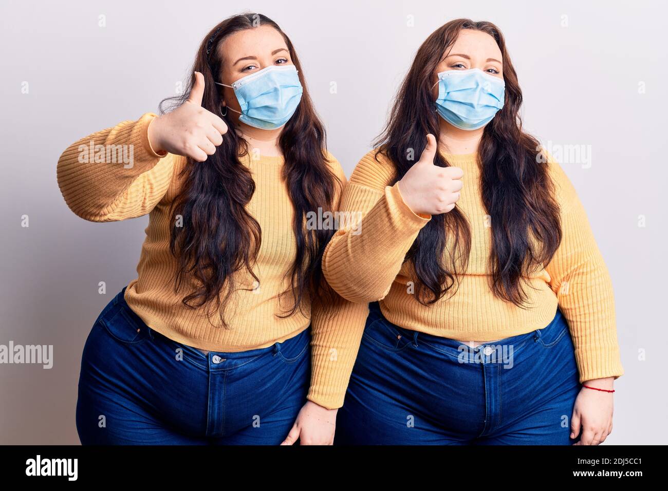 Young plus size twins wearing medical mask doing happy thumbs up ...
