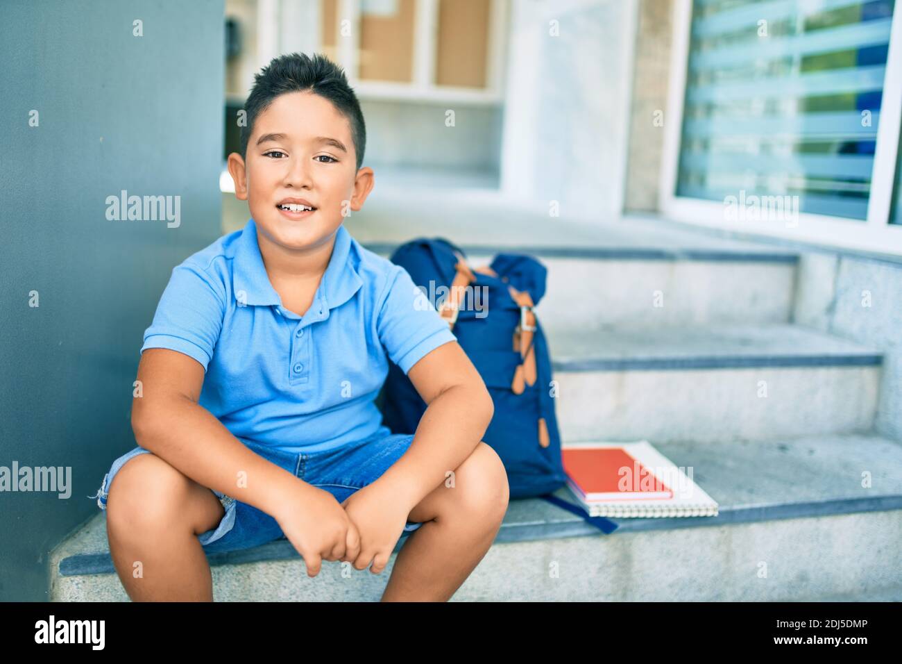 Adorable student boy smiling happy sitting on the stairs at school ...