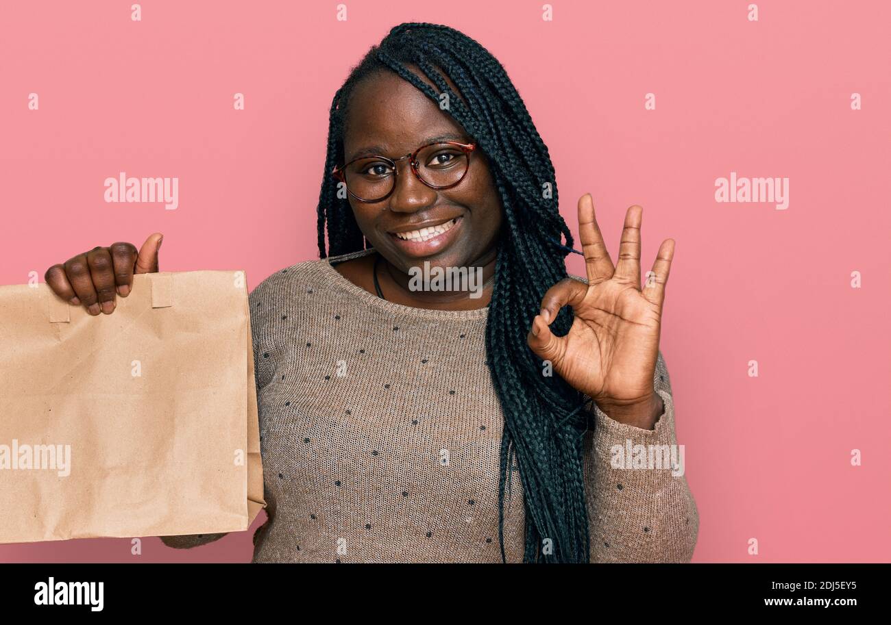 Young black woman with braids holding take away paper bag doing ok sign ...