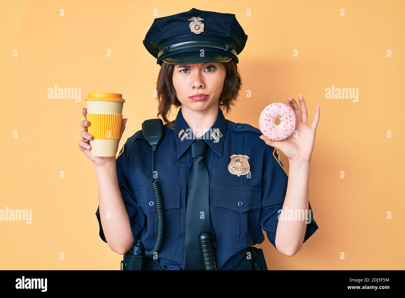 Young beautiful woman wearing police uniform holding donut and take ...