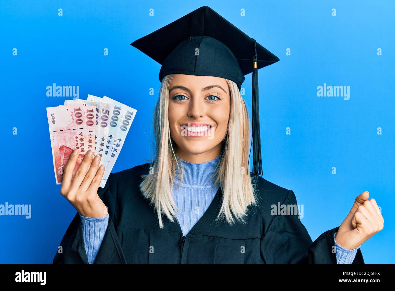 Beautiful blonde woman wearing graduation cap and ceremony robe holding ...