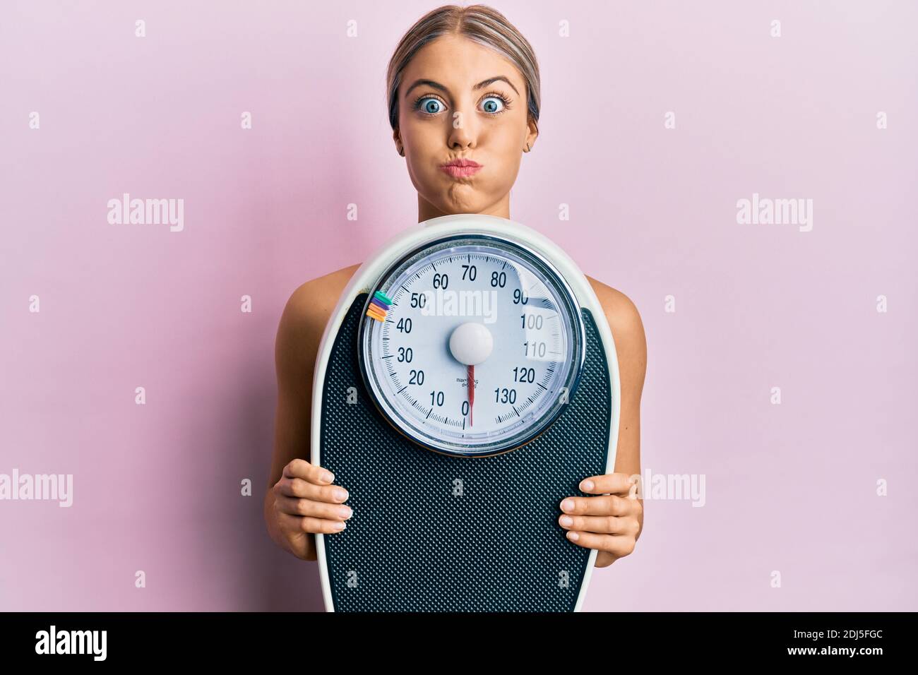 Beautiful blonde woman holding weight machine to balance weight loss ...