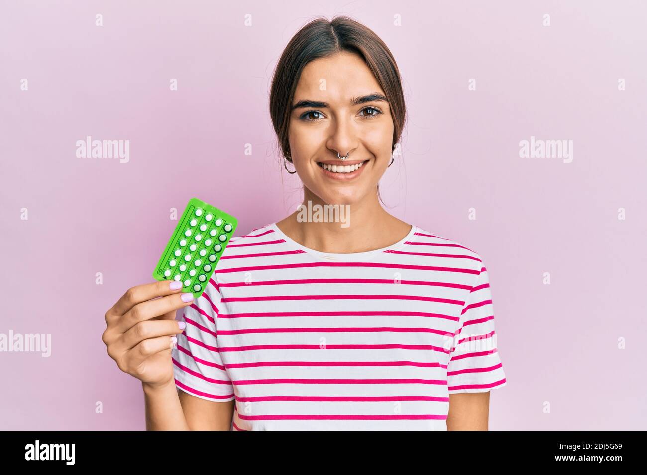 Young hispanic woman holding birth control pills looking positive and ...