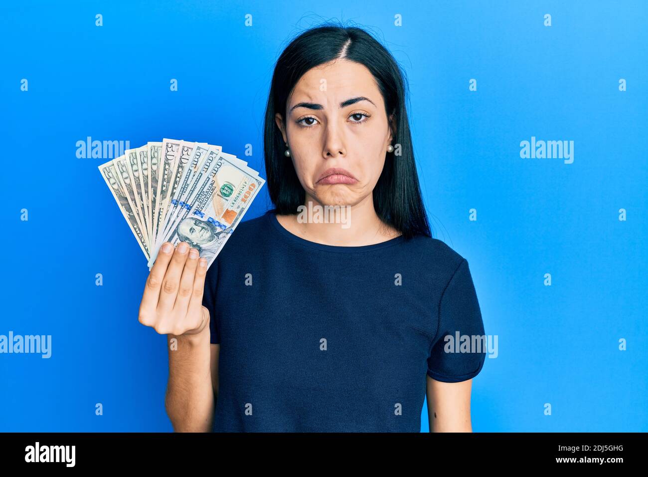 Beautiful young woman holding dollars depressed and worry for distress ...