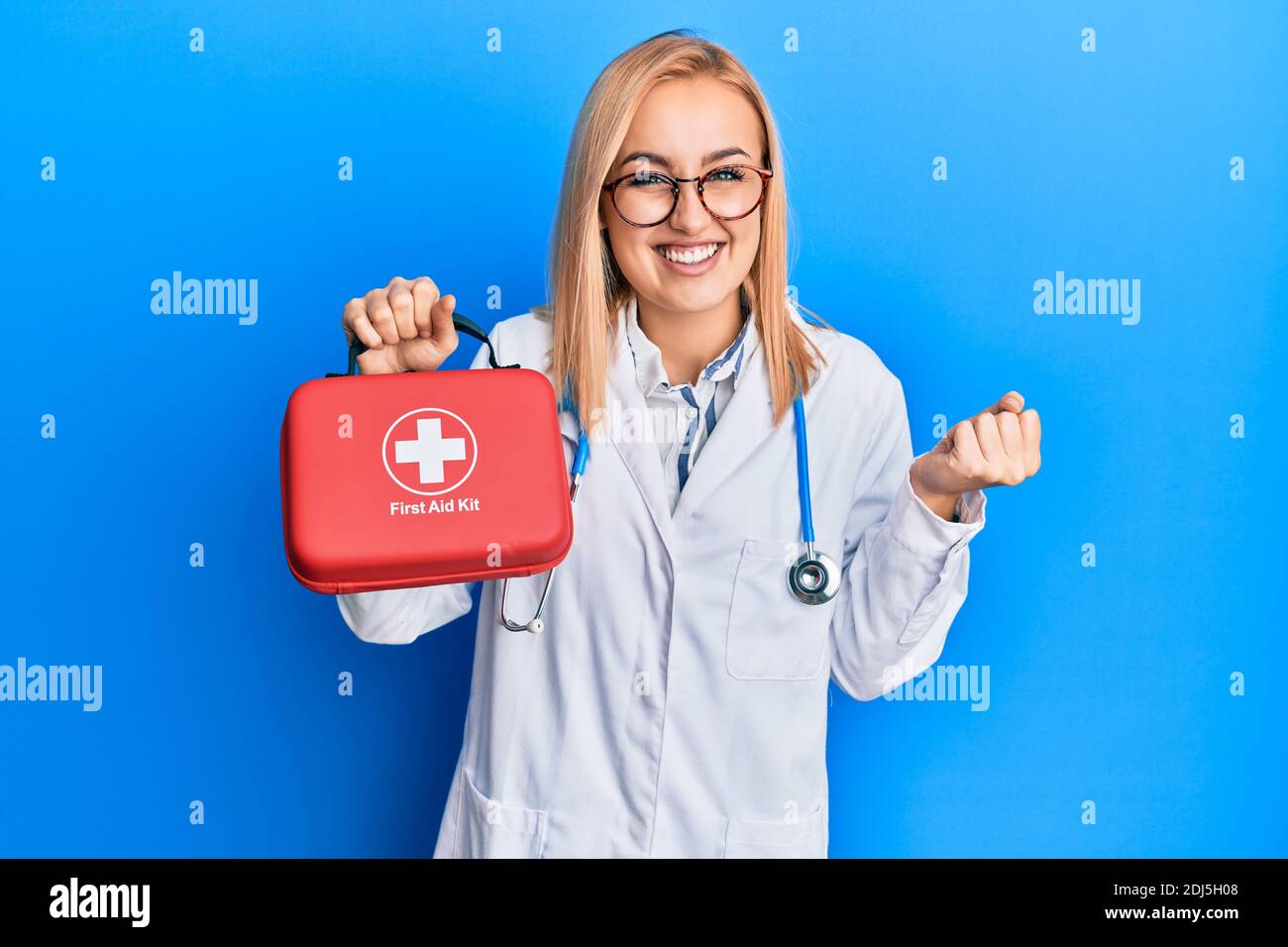 Beautiful caucasian doctor woman holding first aid kit screaming proud ...