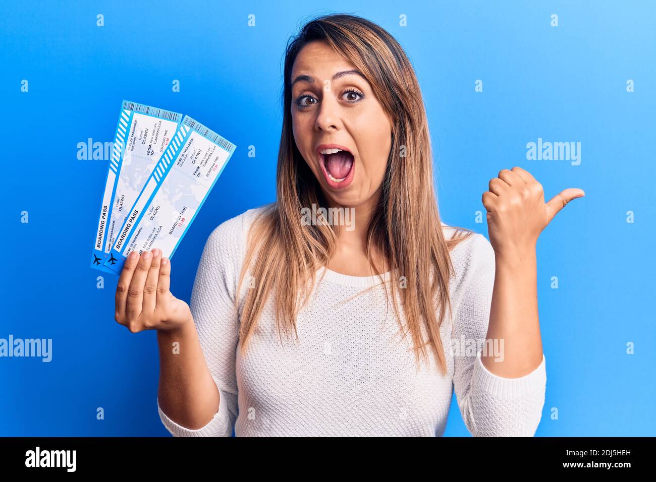 Young beautiful woman holding airline boarding pass pointing thumb up ...