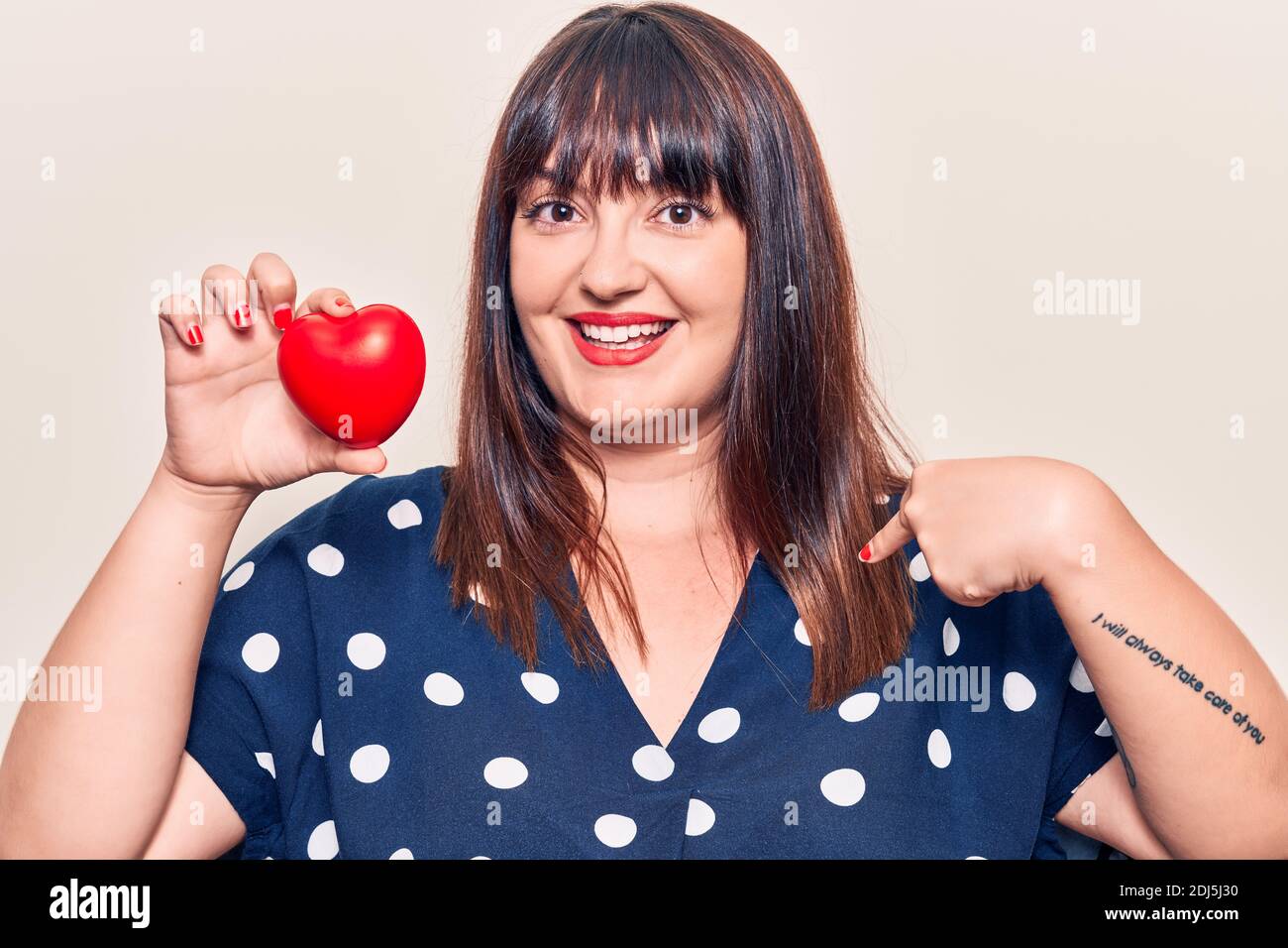 Young plus size woman holding heart pointing finger to one self smiling ...