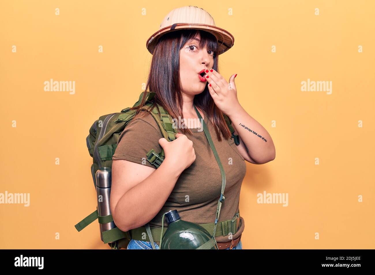 Young plus size woman wearing explorer hat and backpack covering mouth ...