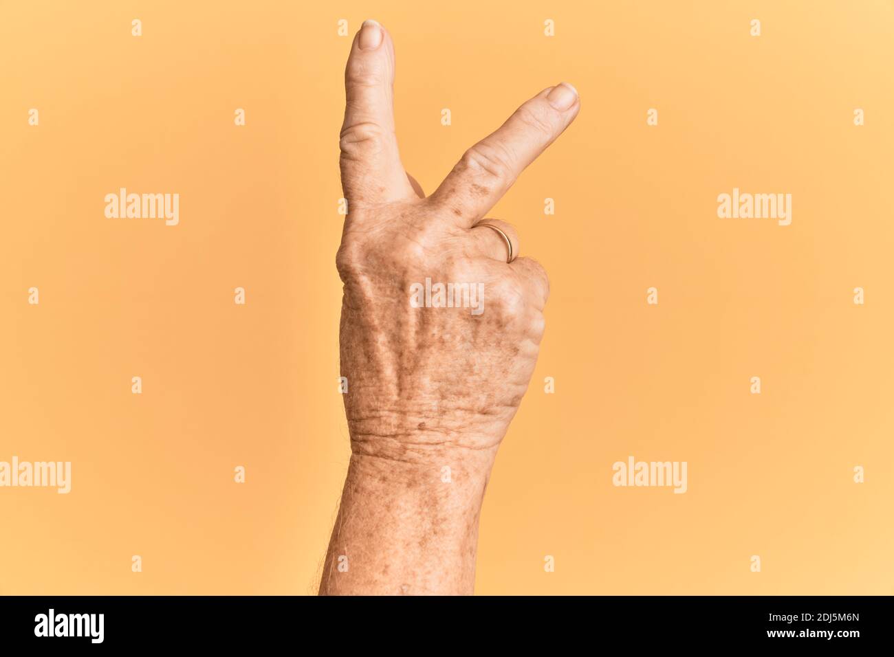 Senior caucasian hand over yellow isolated background counting number 2 ...