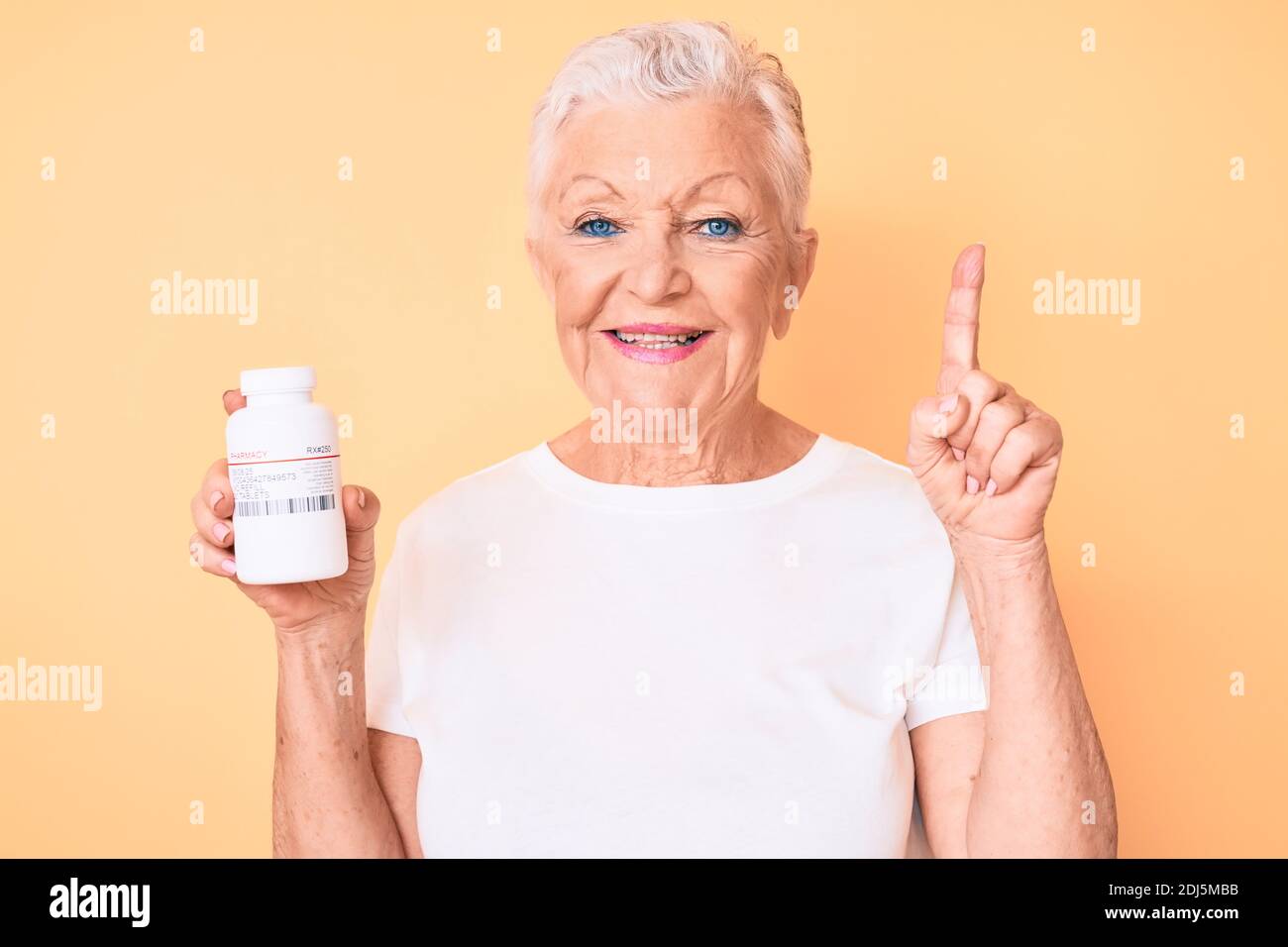 Senior beautiful woman with blue eyes and grey hair holding pills ...