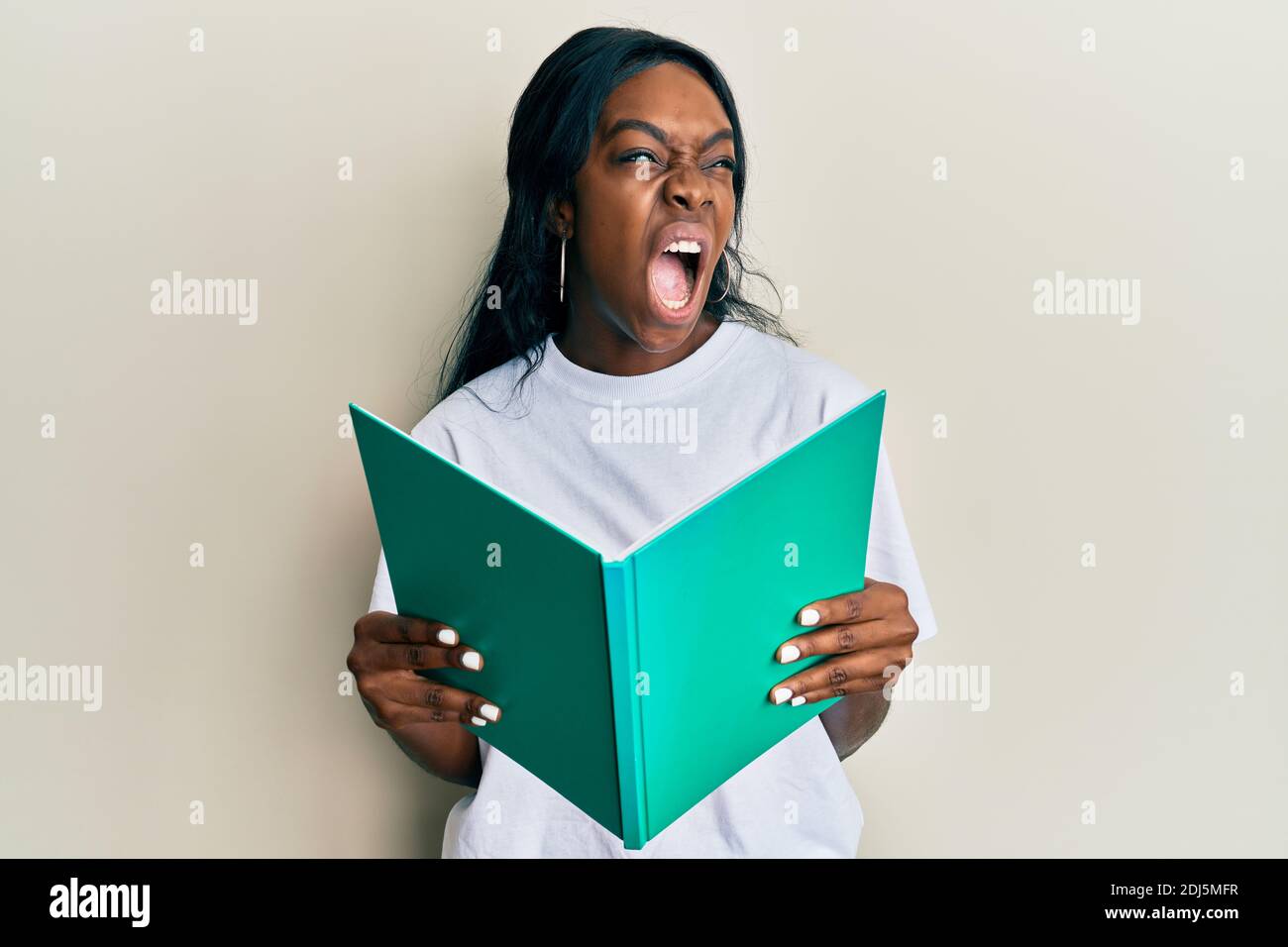 Young african american woman reading book angry and mad screaming ...