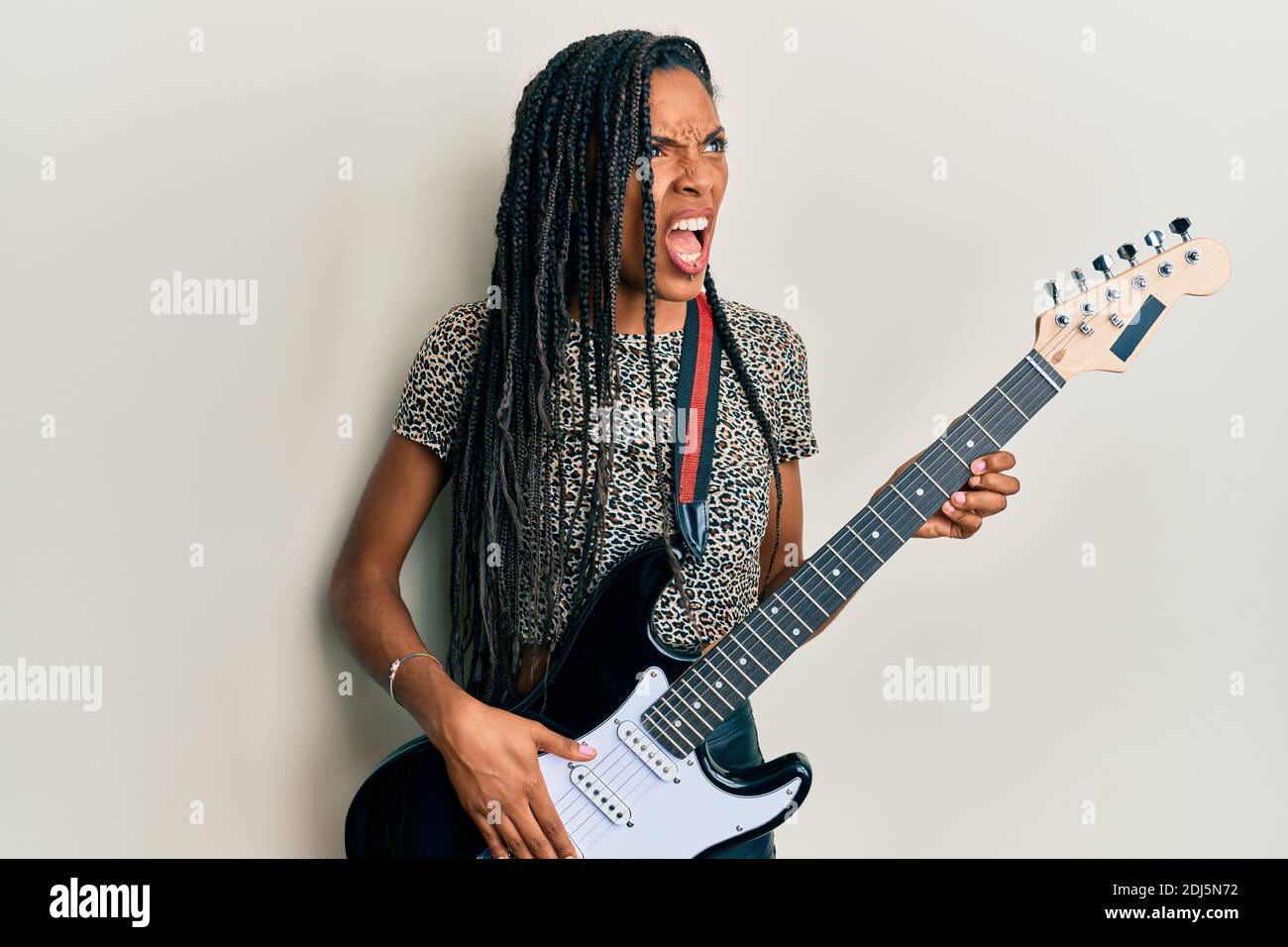 African american woman playing electric guitar angry and mad screaming ...