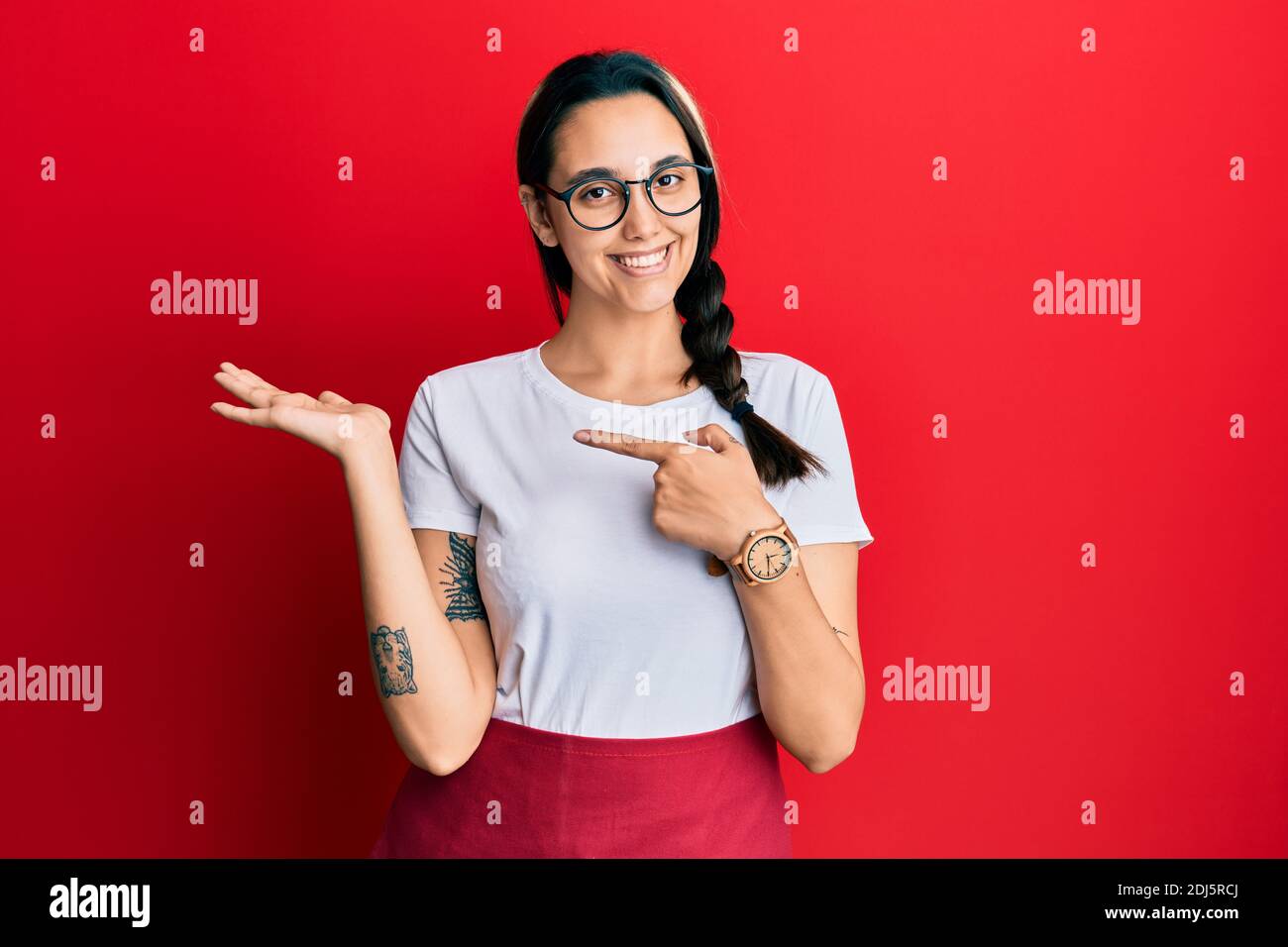 Young hispanic woman wearing professional waitress apron amazed and ...
