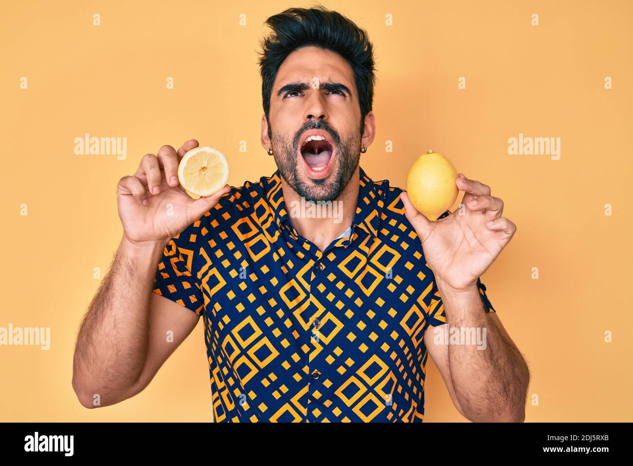 Handsome hispanic man with beard holding lemon angry and mad screaming ...