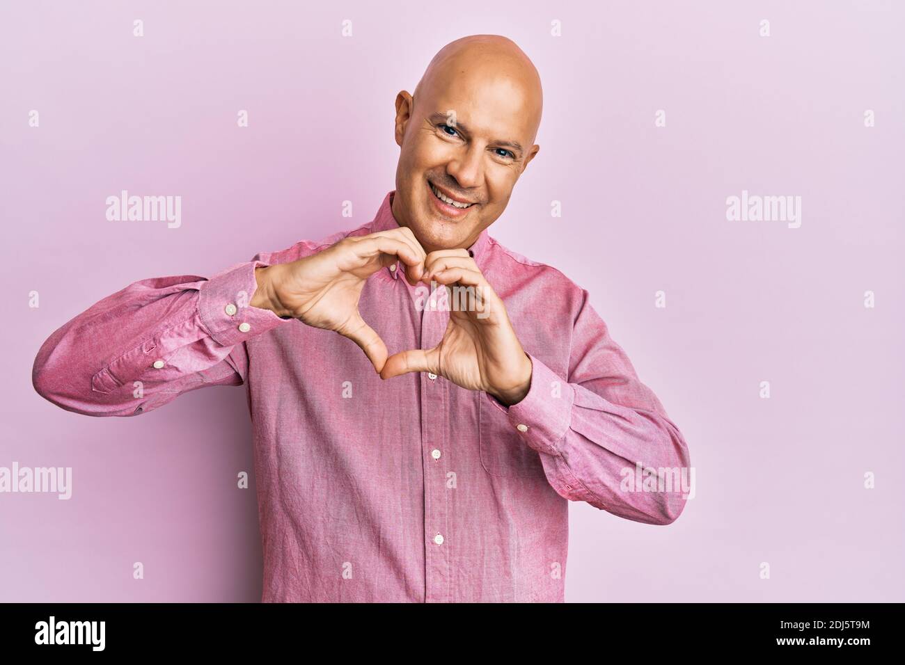 Middle age bald man wearing pink business shirt smiling in love doing ...