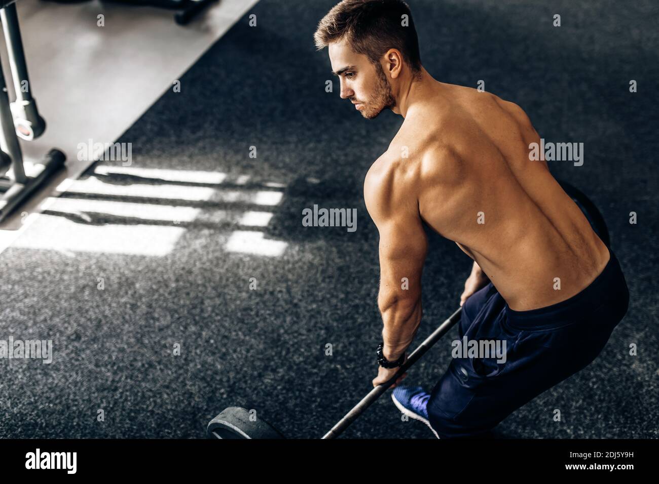 Muscular young man works out with a barbell in the gym. Athletic man ...
