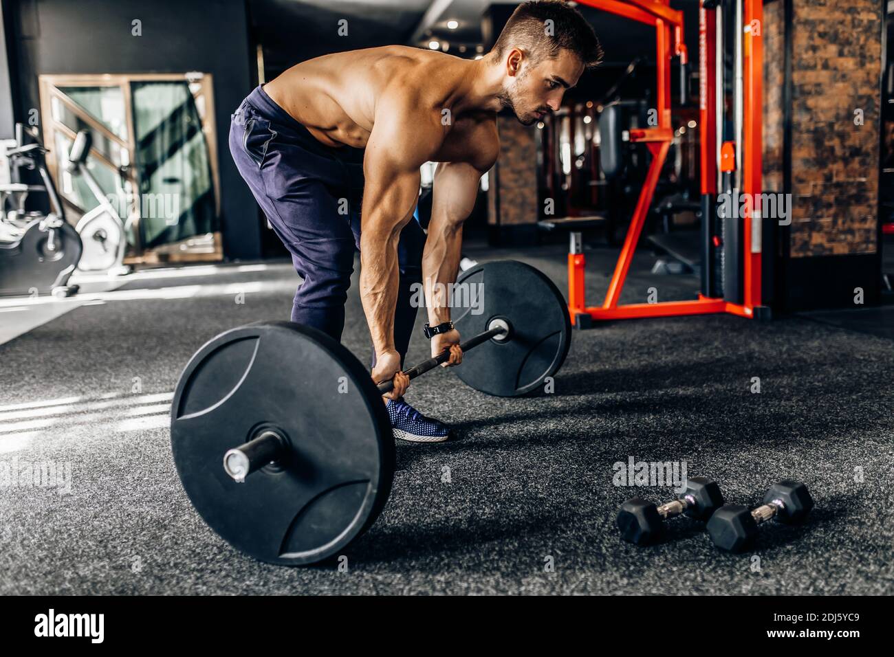 Muscular young man works out with a barbell in the gym. Athletic man ...