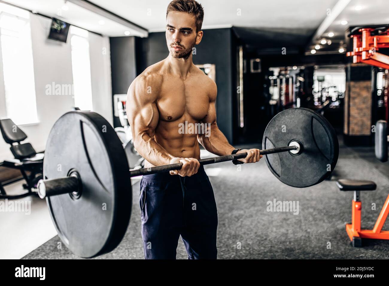 Muscular young man works out with a barbell in the gym. Athletic man ...